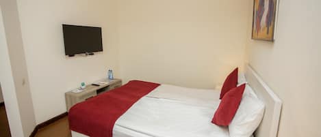Quarto de hotel com cama, televisão de tela plana na parede, mesa de cabeceira com garrafa de água e um quadro na parede.