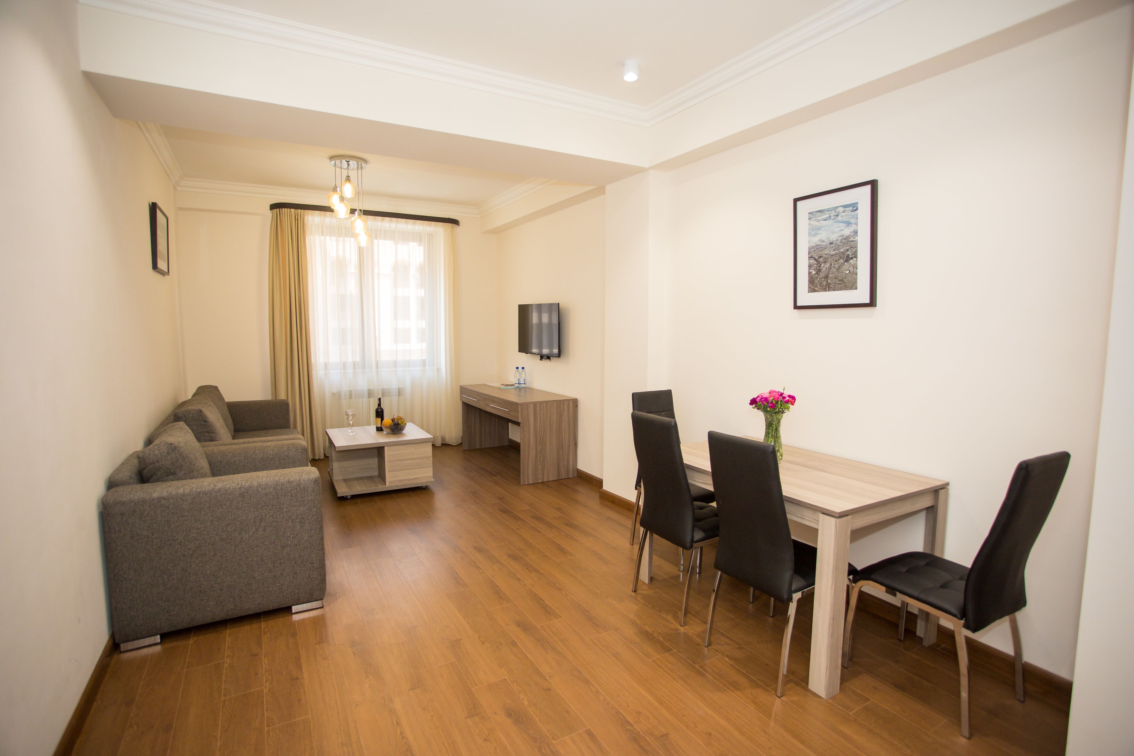 Uma sala de estar moderna com sofá, mesa de jantar com cadeiras, televisão na parede e janela com cortinas.