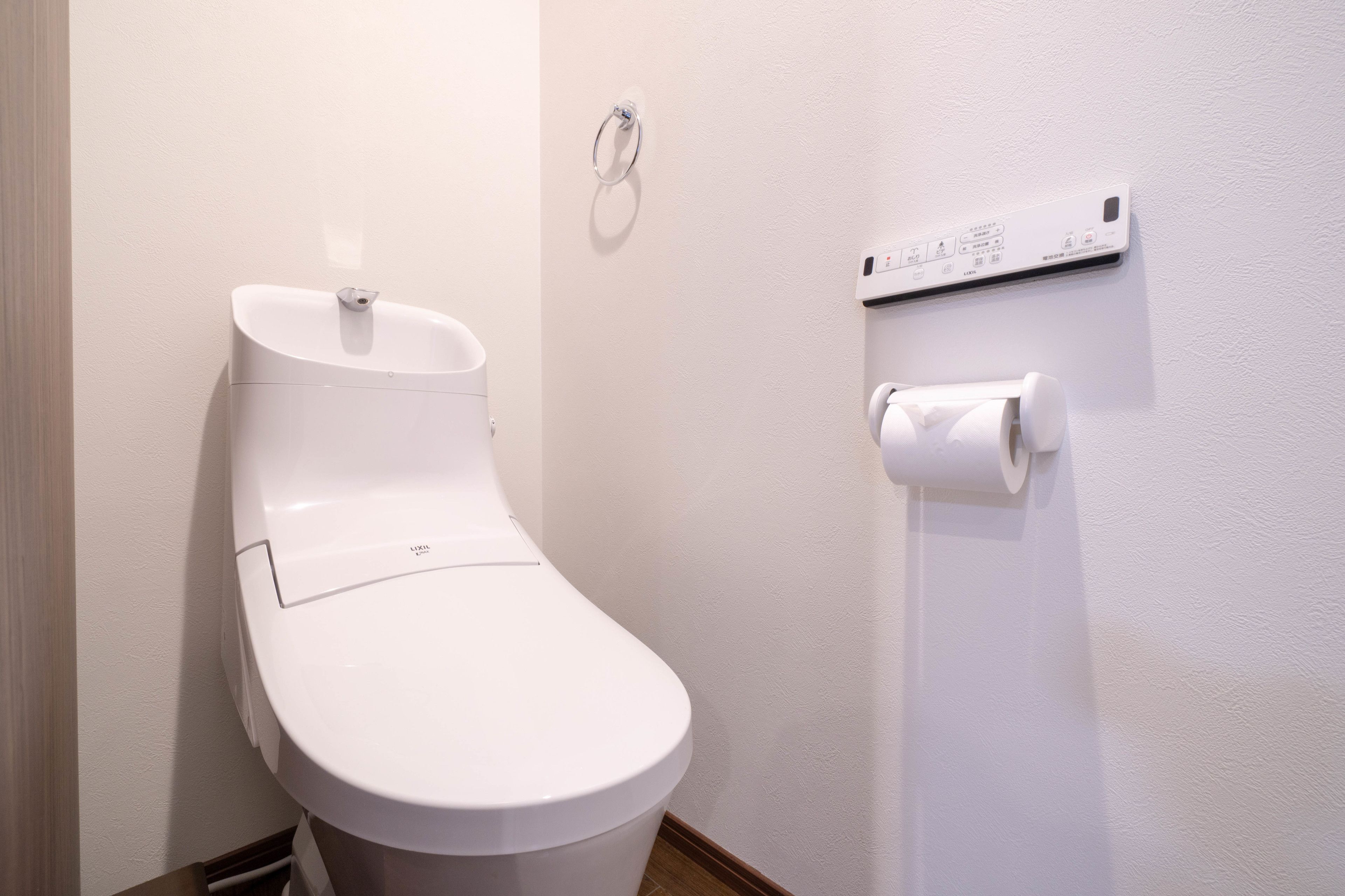 Casa de banho moderna com painel de controlo, suporte de papel higiénico e botão de descarga fixado na parede.