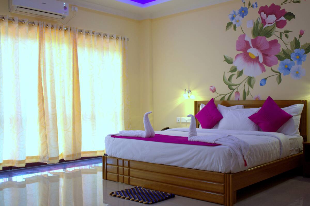 Quarto de hotel com uma cama, cortinas, um mural floral na parede e um abajur.