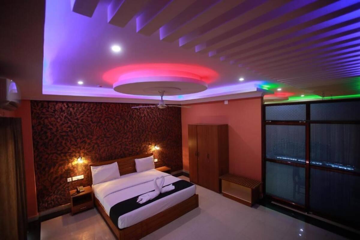 Quarto de hotel moderno com cama de madeira, ventilador de teto e uma janela grande com vista.
