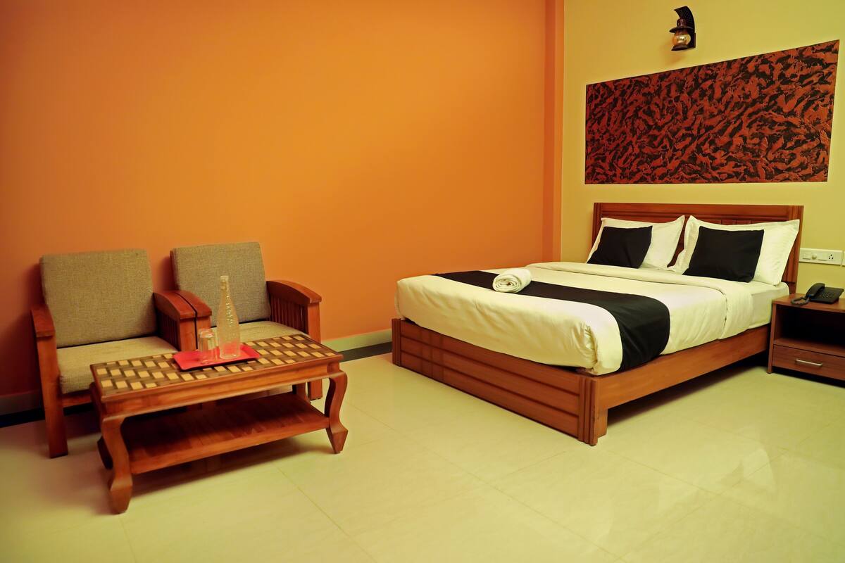 Quarto de hotel com cama, duas cadeiras, uma mesa de madeira e um tapeçário na parede.