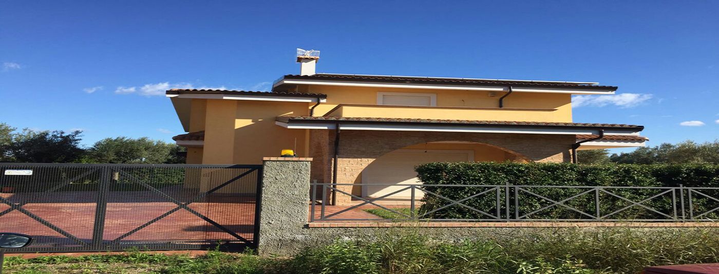 Um edifício de dois andares com fachada amarela, portão fechado e um pequeno jardim.