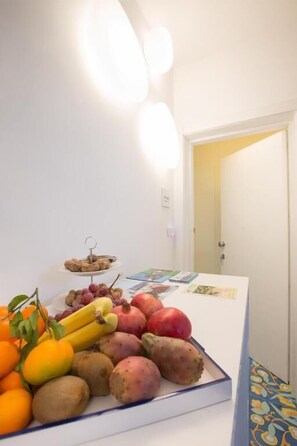 Uma bancada de cozinha com frutas e legumes variados, um pequeno prato com biscoitos e uma porta ao fundo.