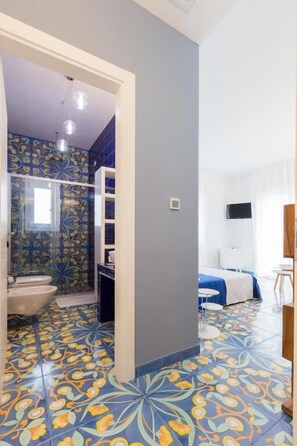 Casa de banho com chuveiro, sanita e lavatório, e quarto com cama e televisão.