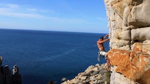 Uma pessoa escala um penhasco rochoso com vista para o oceano.