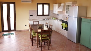 Uma cozinha com mesa de jantar, cadeiras, fogão, geladeira e armários.