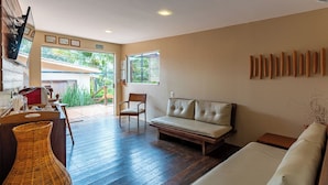 Quarto com piso de madeira, um sofá, uma cadeira, um cesto de vime e uma televisão fixada na parede.