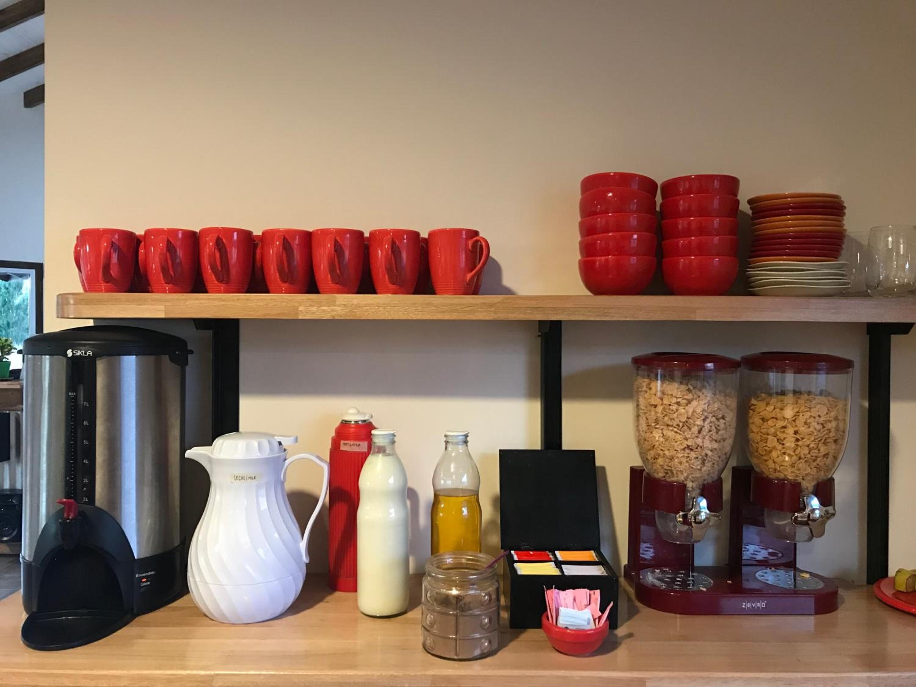Uma bancada de cozinha com cafeteira, jarra de leite, dosador de açúcar e dosador de cereais.