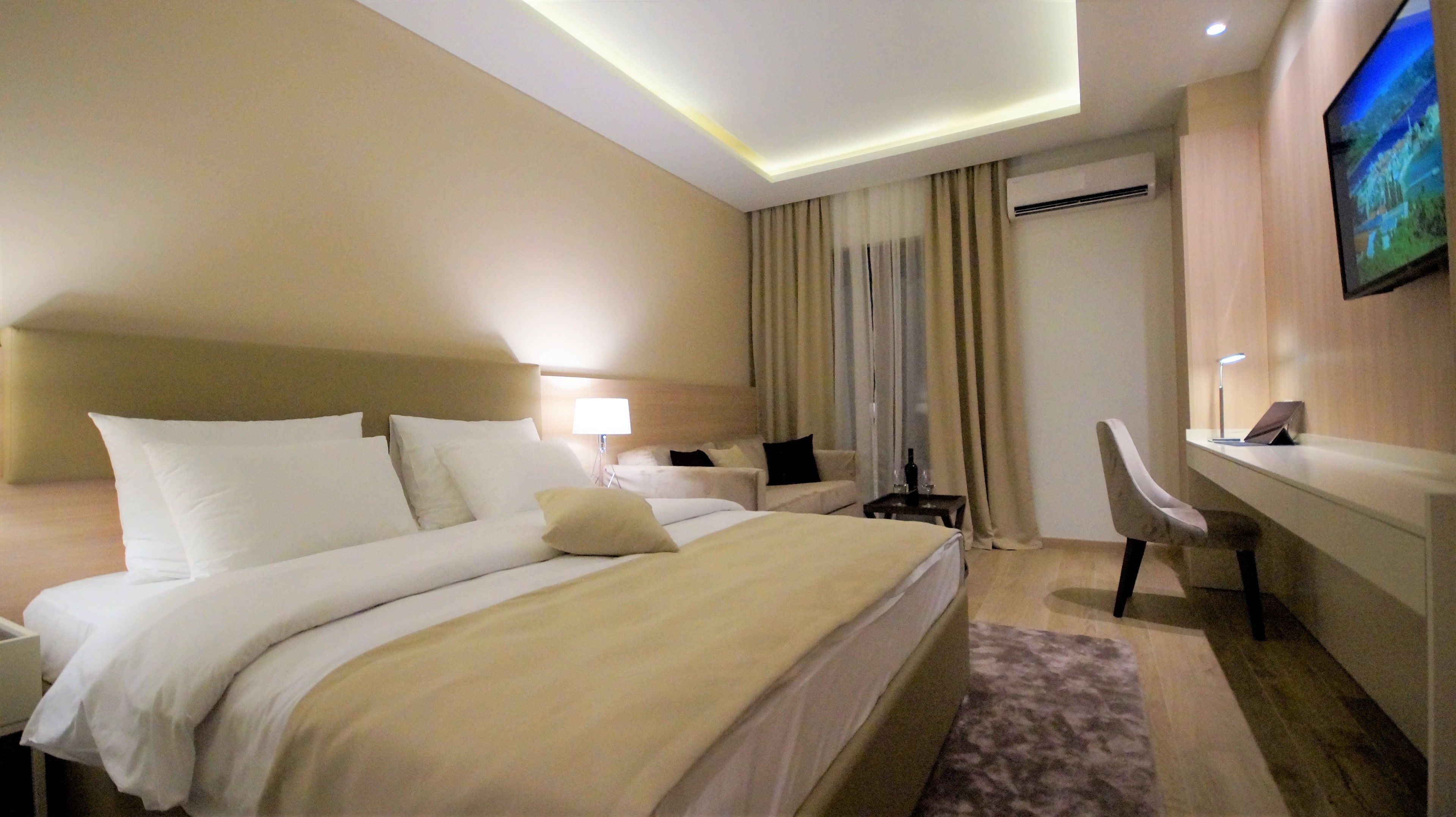 Quarto de hotel com uma cama grande, uma escrivaninha com cadeira, TV fixada na parede e ar condicionado.
