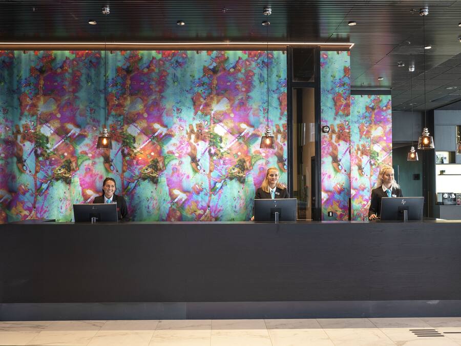 Uma receção com três computadores, um grande mural abstrato e luminárias pendentes.