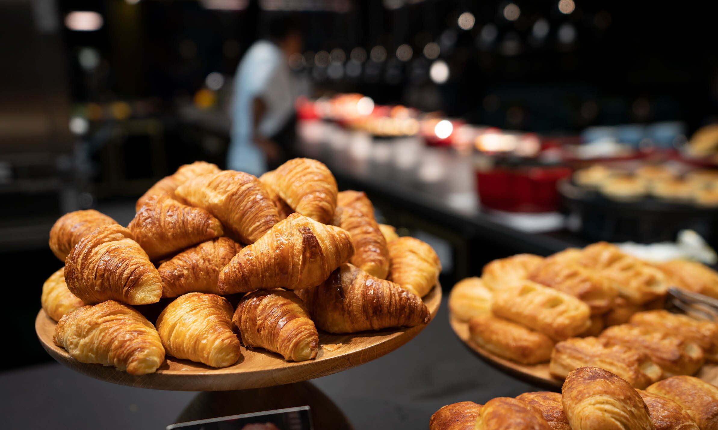 Uma variedade de doces e pastelaria, incluindo croissants, apresentados em tábuas de madeira.
