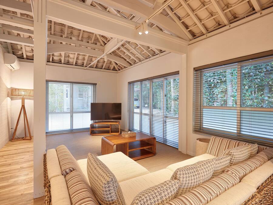 Uma sala de estar espaçosa com teto alto, janelas amplas, um conjunto de sofás, uma TV e uma mesa de centro de madeira.