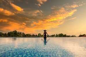 Uma pessoa de fato de banho em uma piscina, com o pôr do sol ao fundo.