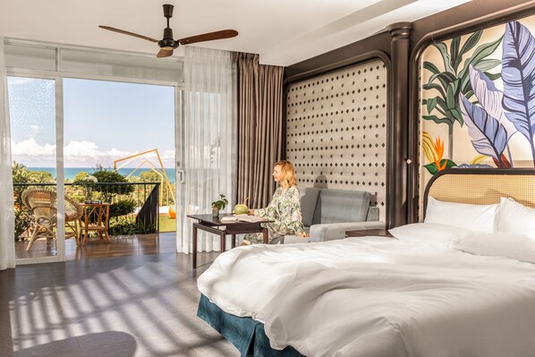 Quarto de hotel com uma cama, uma escrivaninha, uma cadeira e vista para o oceano.