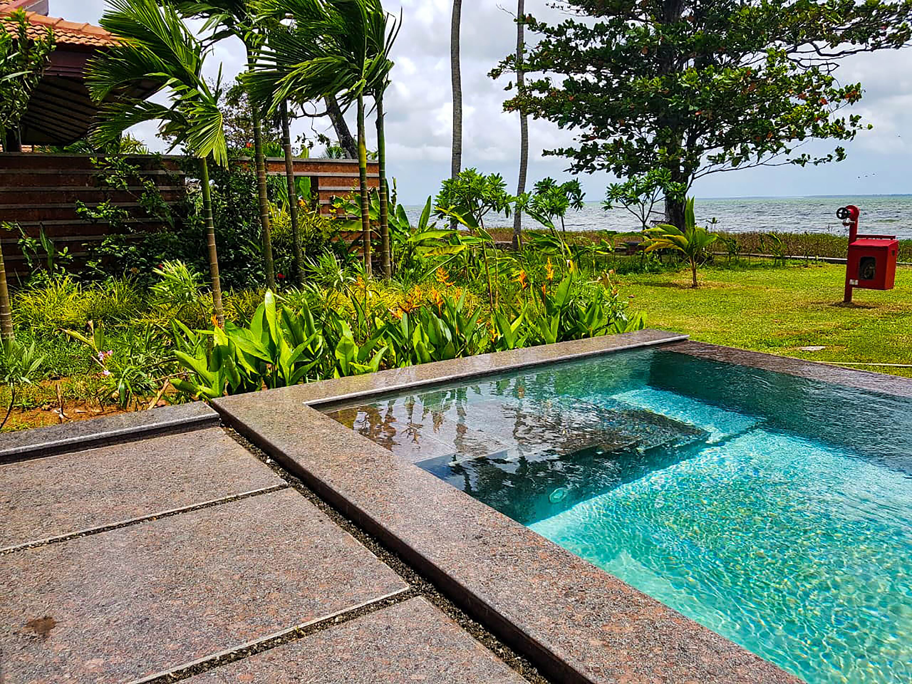 Uma piscina com  água azul cristalina, rodeada por vegetação exuberante e vista para o oceano.