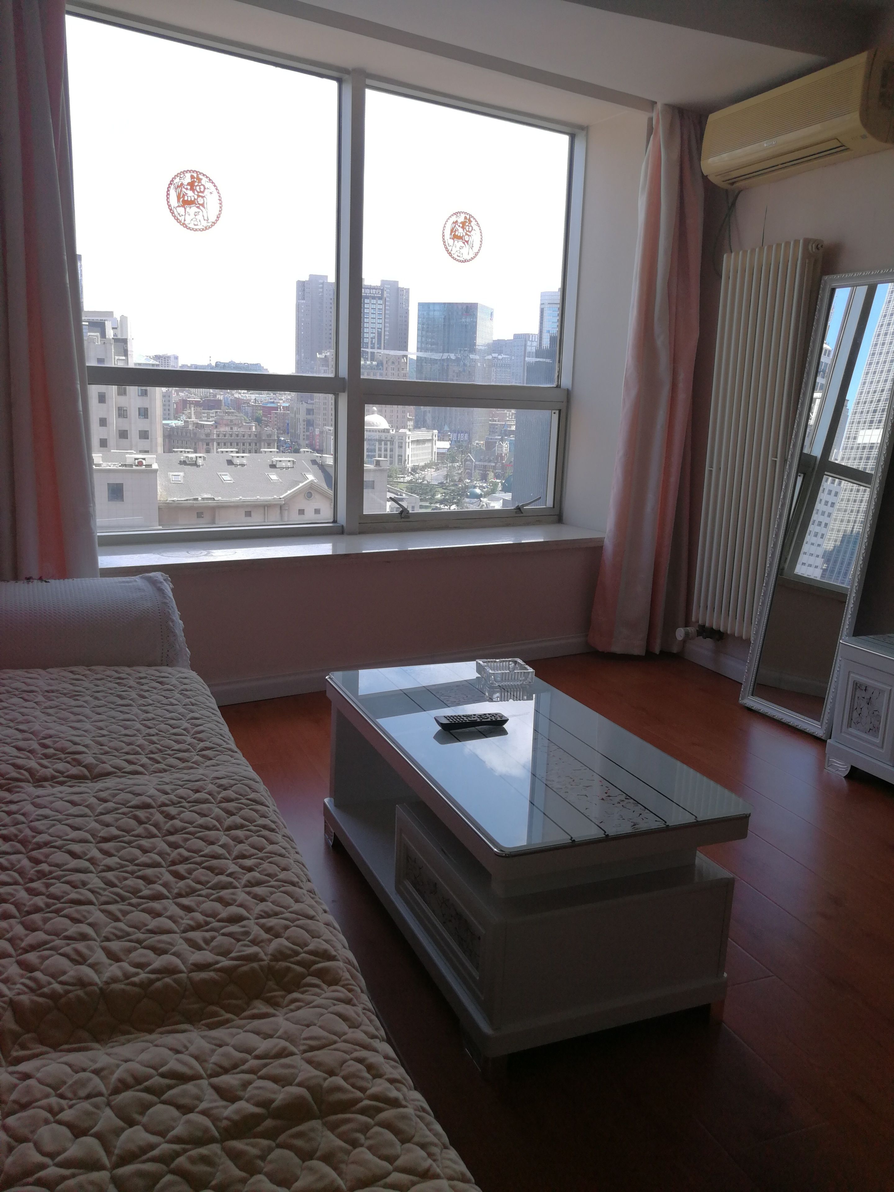 Uma sala de estar moderna com uma janela grande, uma mesa de centro de vidro, um sofá e um radiador.