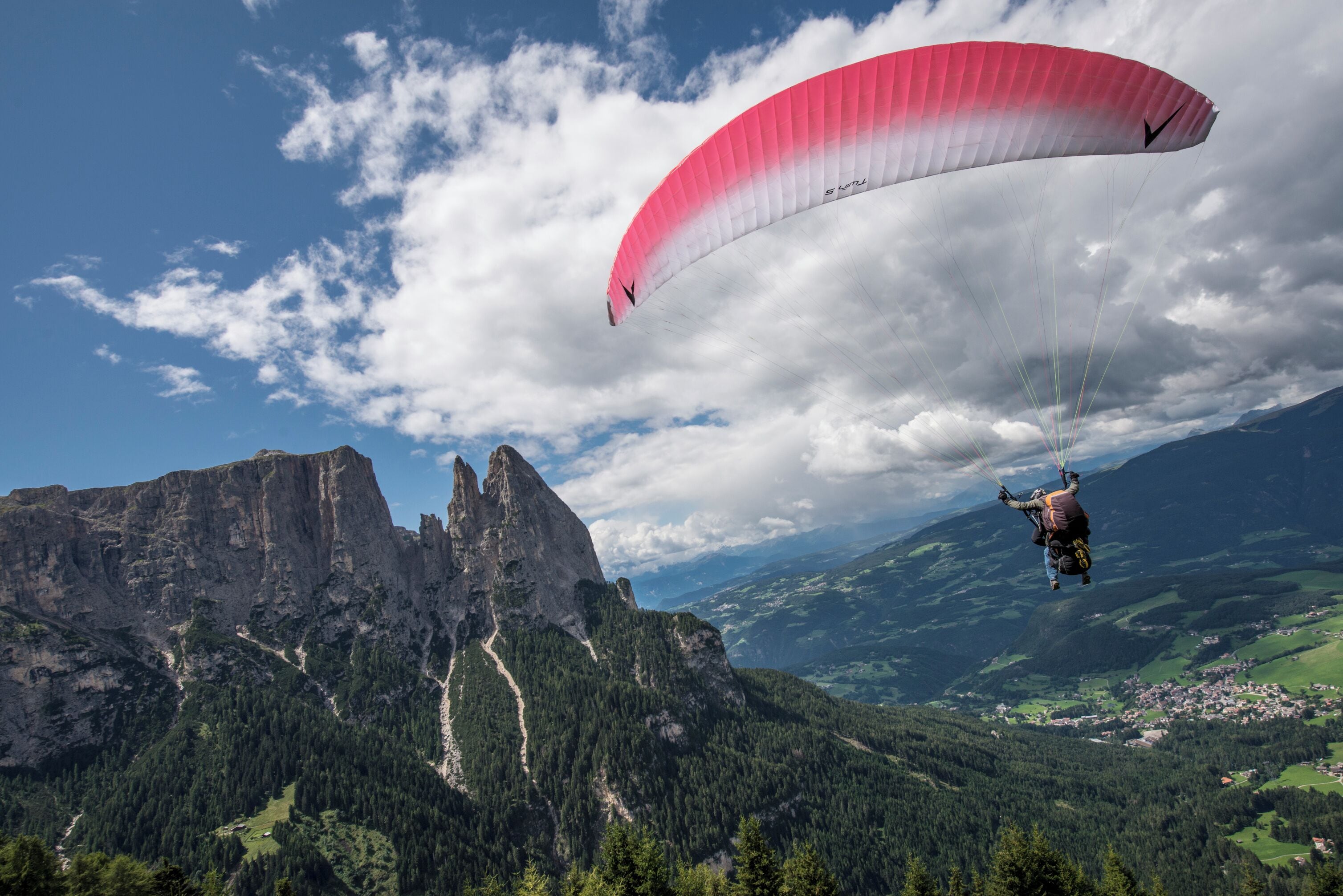 Um parapente sobre uma paisagem montanhosa com uma formação rochosa imponente.