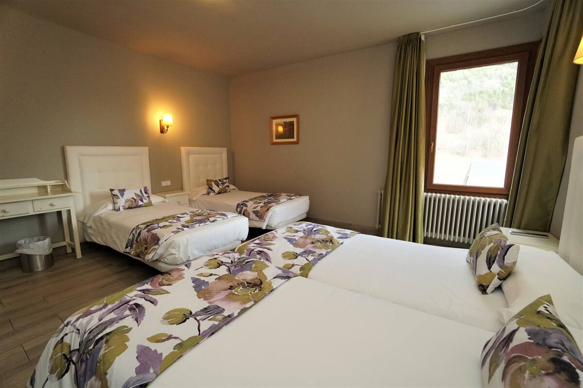 Quarto de hotel com duas camas, uma escrivaninha e uma janela com cortinas.