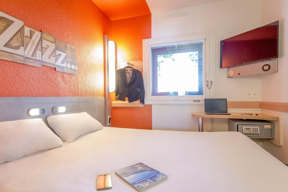 Quarto de hotel com cama, televisão, escrivaninha com um laptop, cofre e janela com vista.