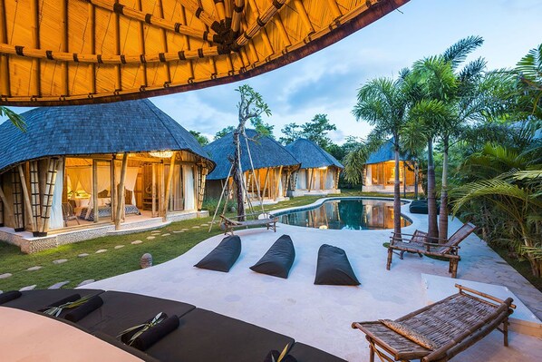 Resort com villas de telhado de palha, piscina e espreguiçadeiras.
