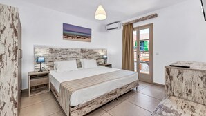 Quarto com cama grande, mesa de cabeceira, abajur, pintura na parede e vista através de uma porta.