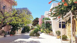 Uma rua estreita, flanqueada por edifícios, plantas em vasos e um banco de madeira.