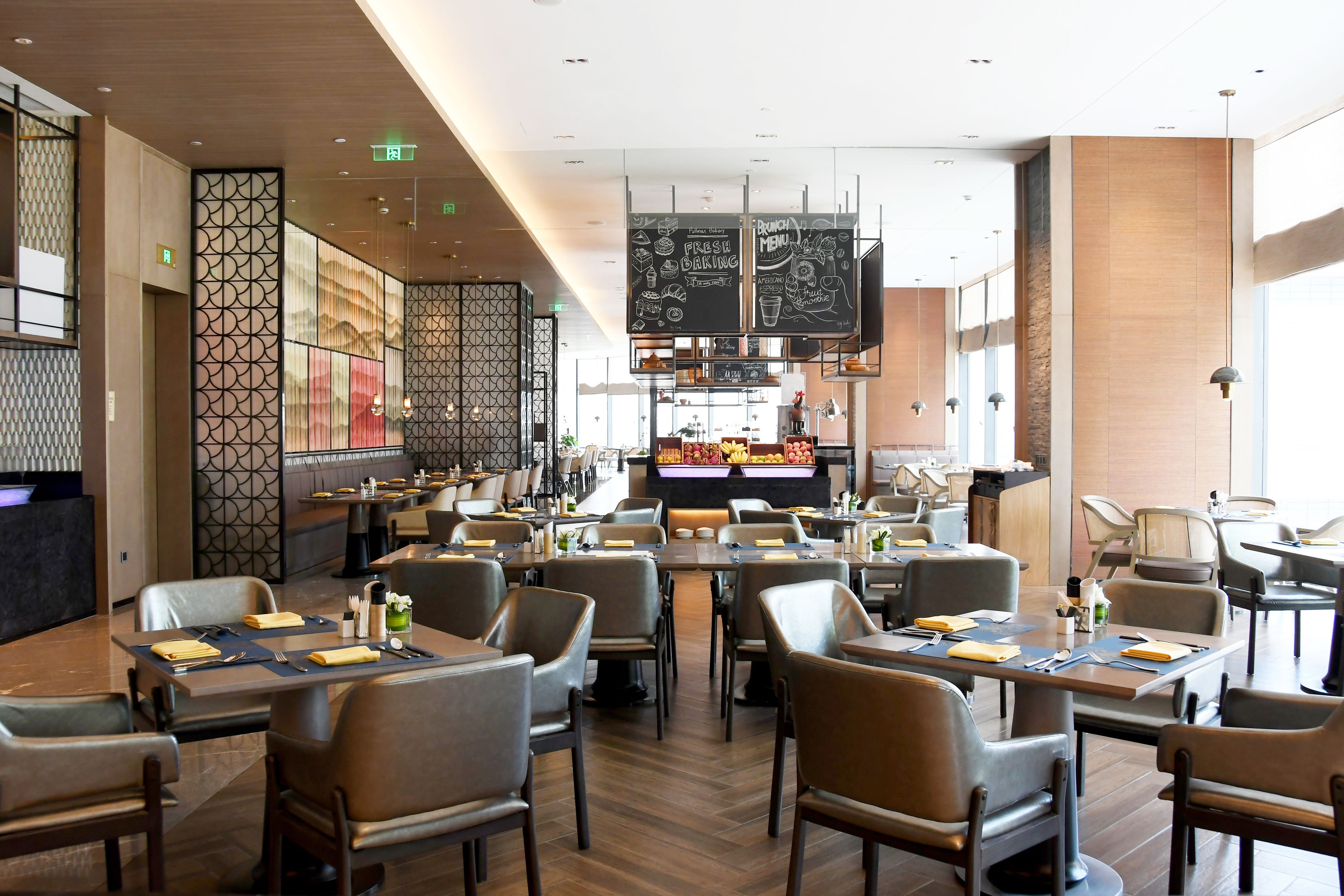 Um restaurante moderno com várias mesas e cadeiras, um balcão central com menu em lousa e painéis decorativos nas paredes.