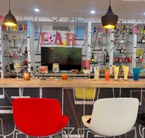 Uma área de bar com televisão, prateleiras cheias de bebidas e duas cadeiras.