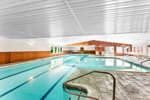 Piscina interna com pistas demarcadas, parede de madeira e chão de pedra.