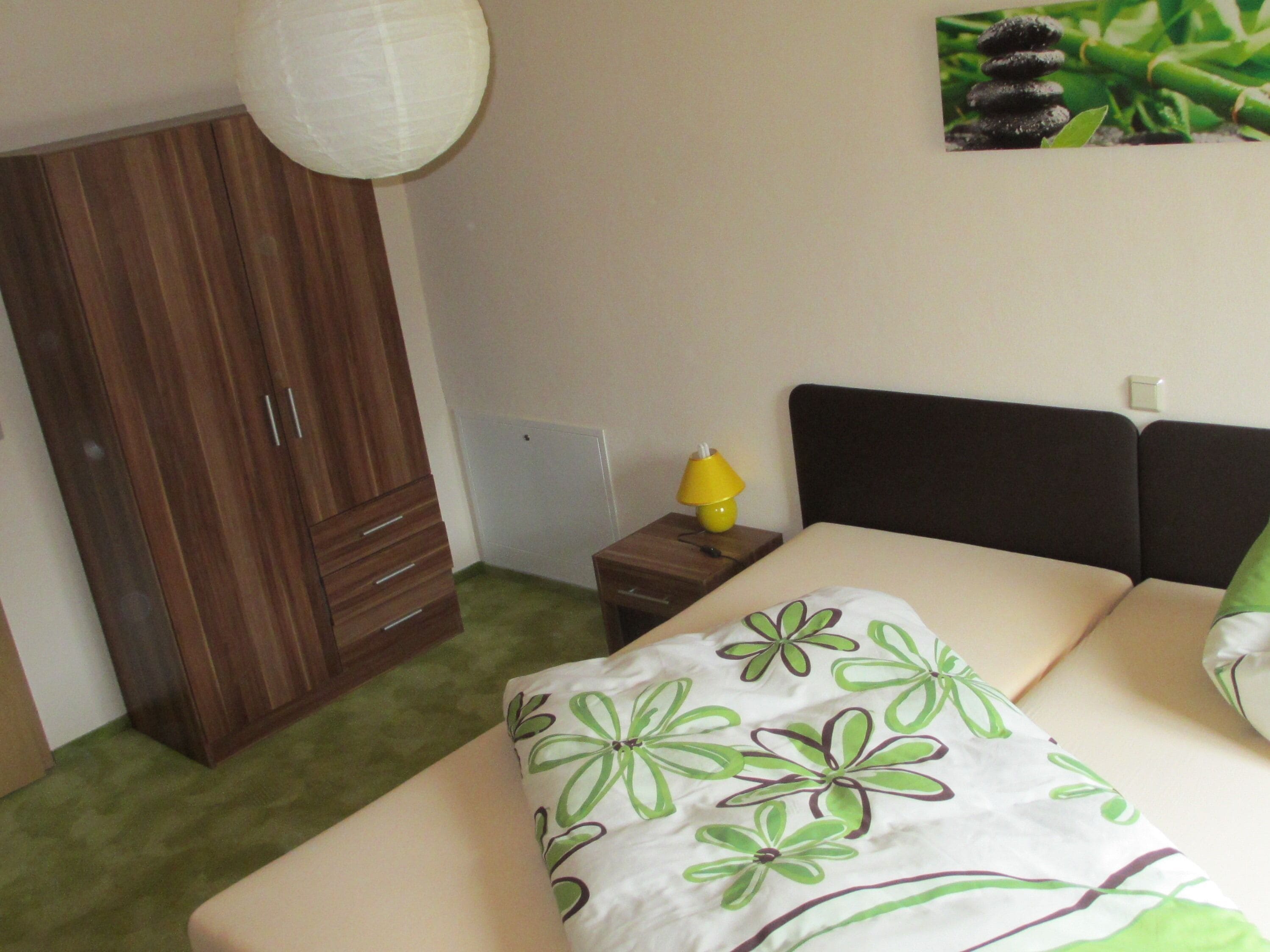 Quarto com cama, mesa de cabeceira, luminária, guarda-roupa e um objeto decorativo na parede.