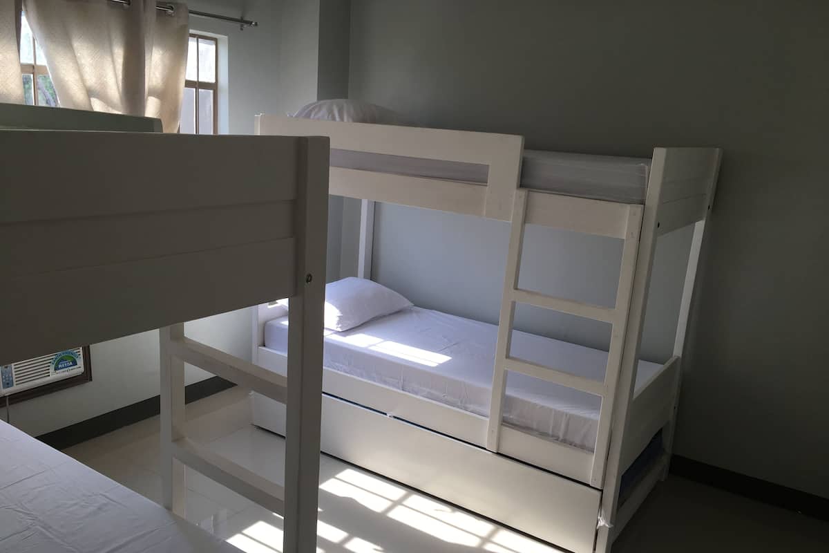 Uma cama beliche num quarto com janela, radiador e uma mesa branca.