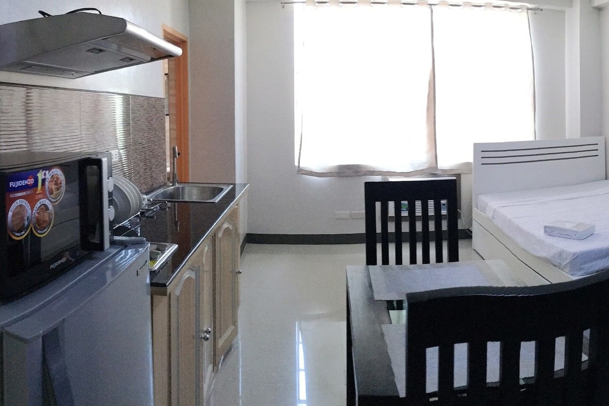 Quarto compacto com cozinha compacta, uma cama, uma cadeira e um quadro na parede.