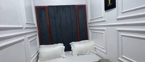 Um quarto pequeno e bem arrumado, com uma cama, travesseiros, um aparelho de ar condicionado e um quadro na parede.