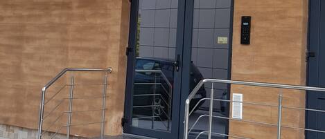 Entrada de um edifício com porta preta, corrimão de metal e um degrau que leva à entrada.