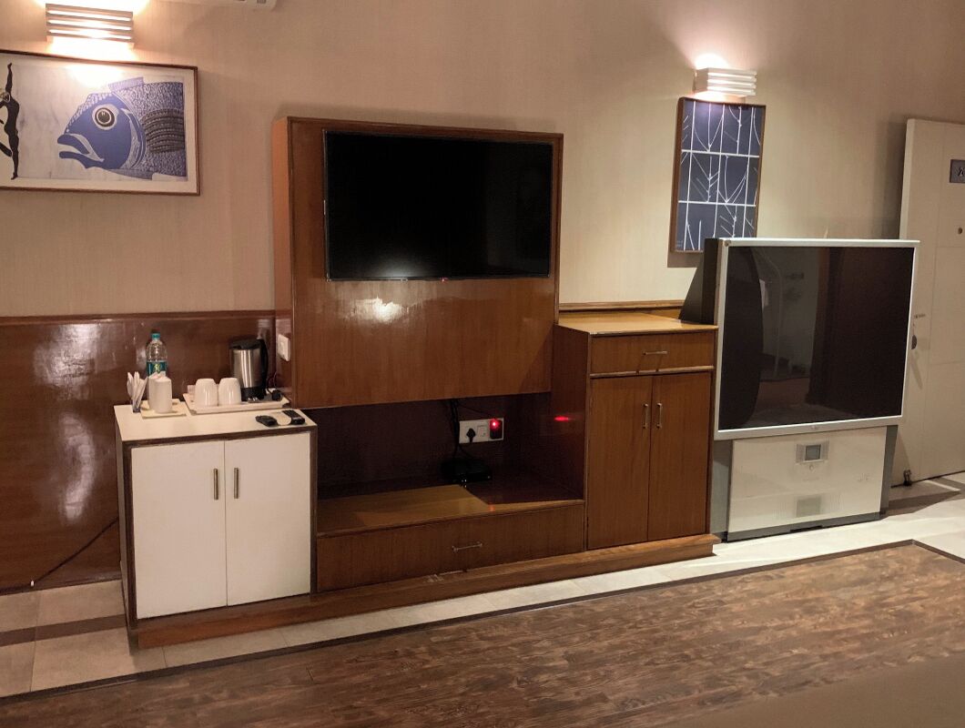 Quarto de hotel moderno com um armário de madeira, uma televisão de tela plana, um refrigerador e uma pequena área de cozinha.