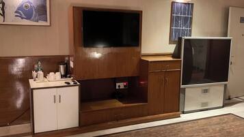 Quarto de hotel moderno com um armário de madeira, uma televisão de tela plana, um refrigerador e uma pequena área de cozinha.