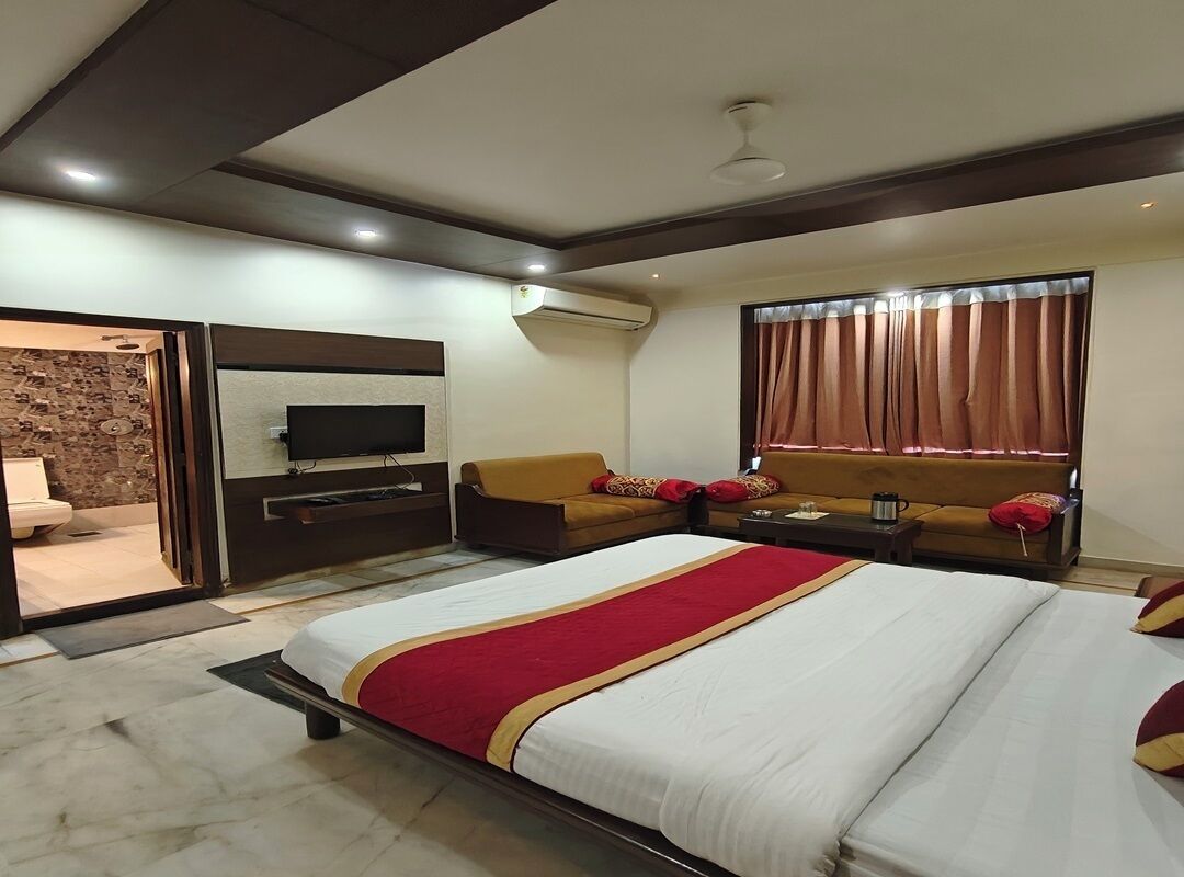 Quarto de hotel com cama grande, sofá, televisão e banheiro visível por uma porta aberta.