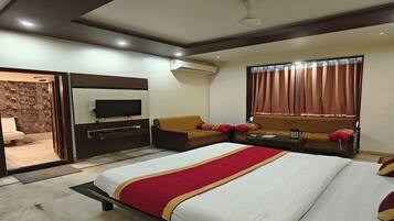 Quarto de hotel com cama grande, sofá, televisão e banheiro visível por uma porta aberta.