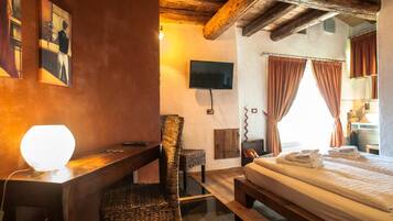 Quarto de hotel acolhedor com uma secretária de madeira, uma cadeira confortável, uma cama com toalhas cuidadosamente dobradas e uma televisão de ecrã plano fixada na parede.