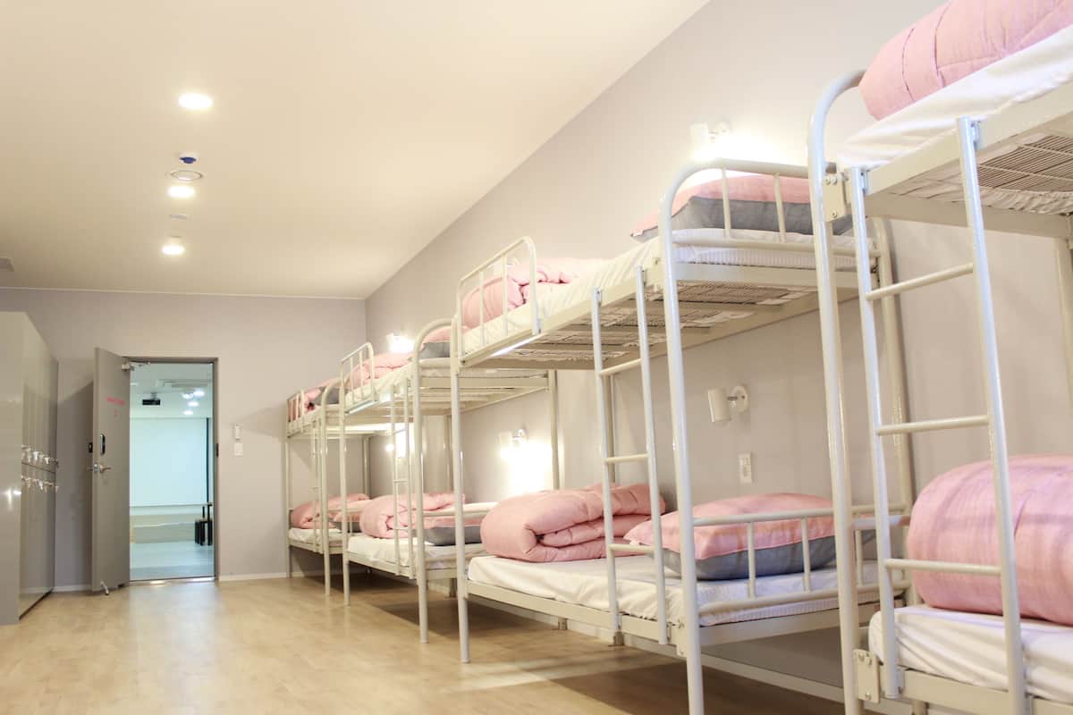 Quarto com beliches, uma porta e piso em tom claro.