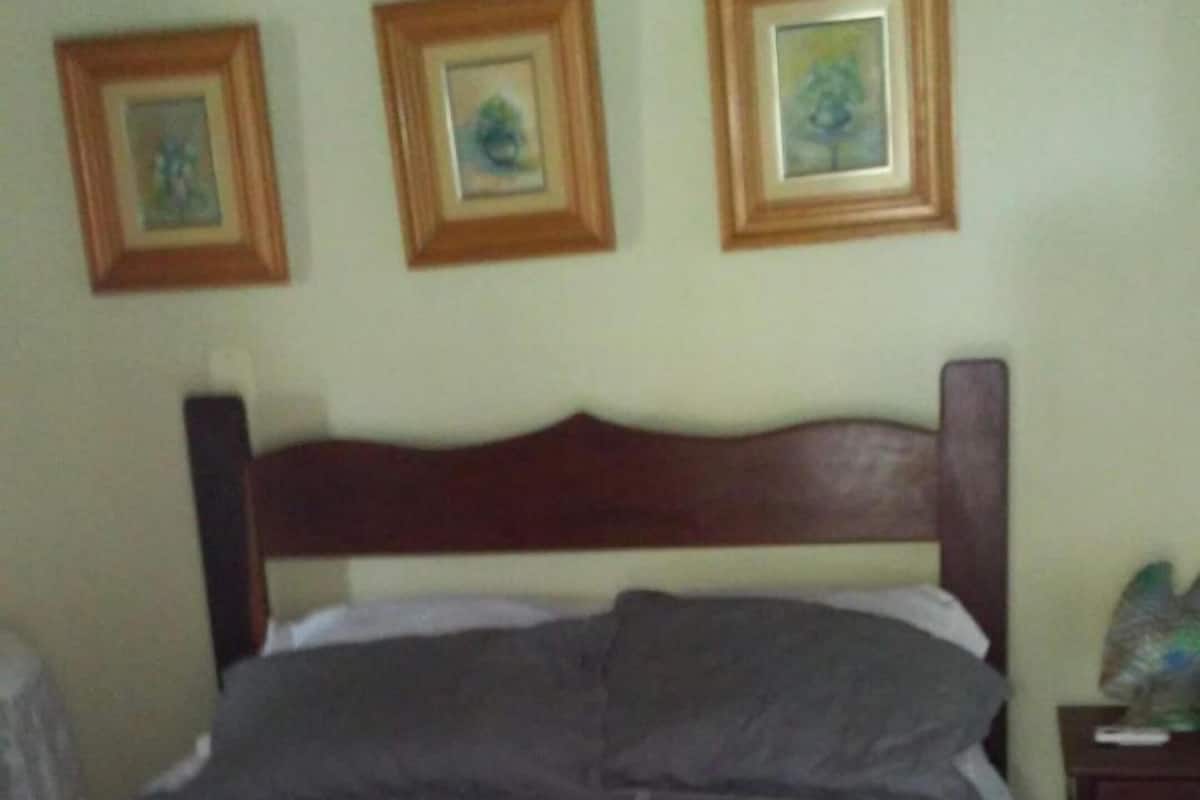 Uma cama com cabeceira de madeira, um cobertor e duas molduras com quadros na parede.