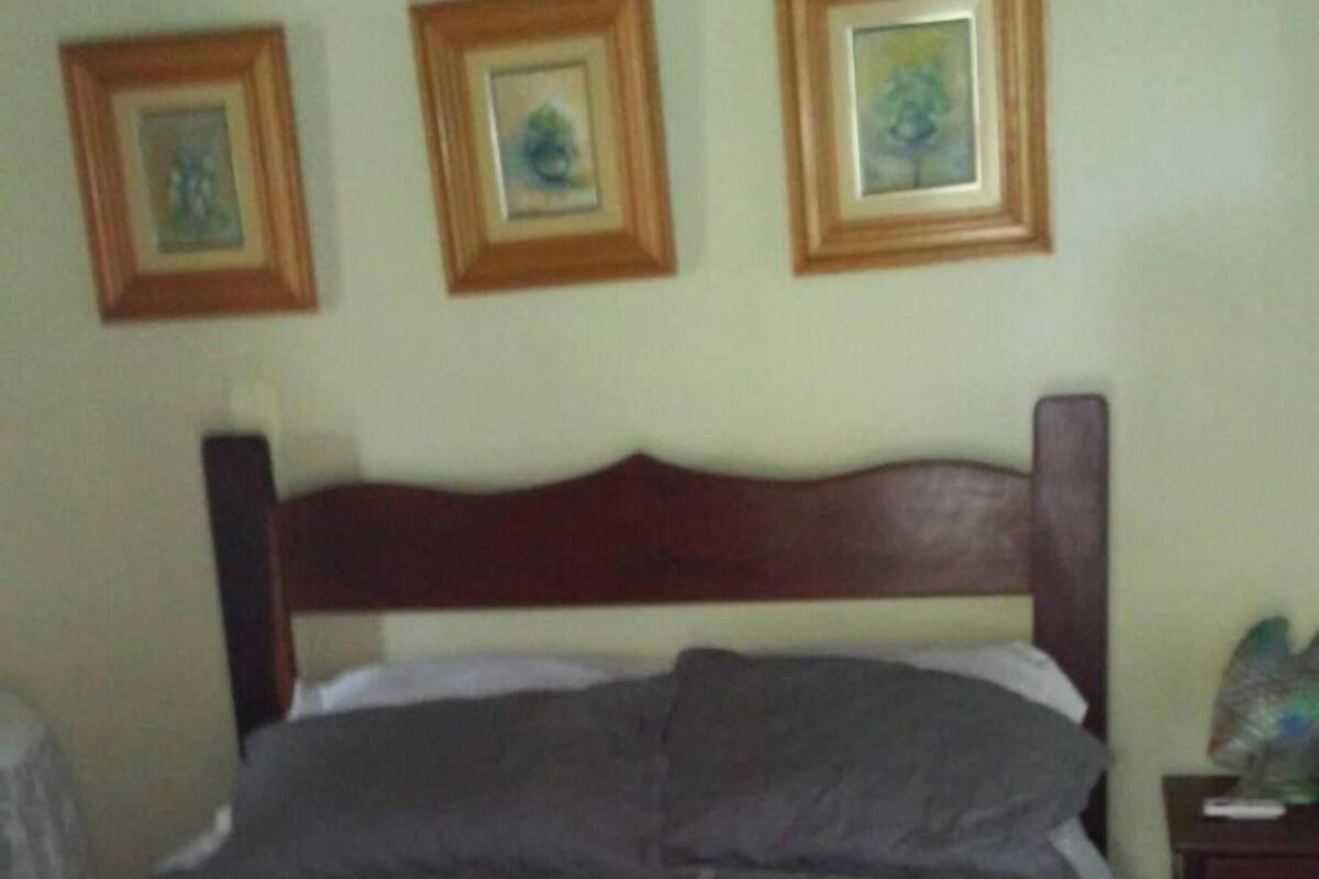 Uma cama com cabeceira de madeira, um cobertor e duas molduras com quadros na parede.