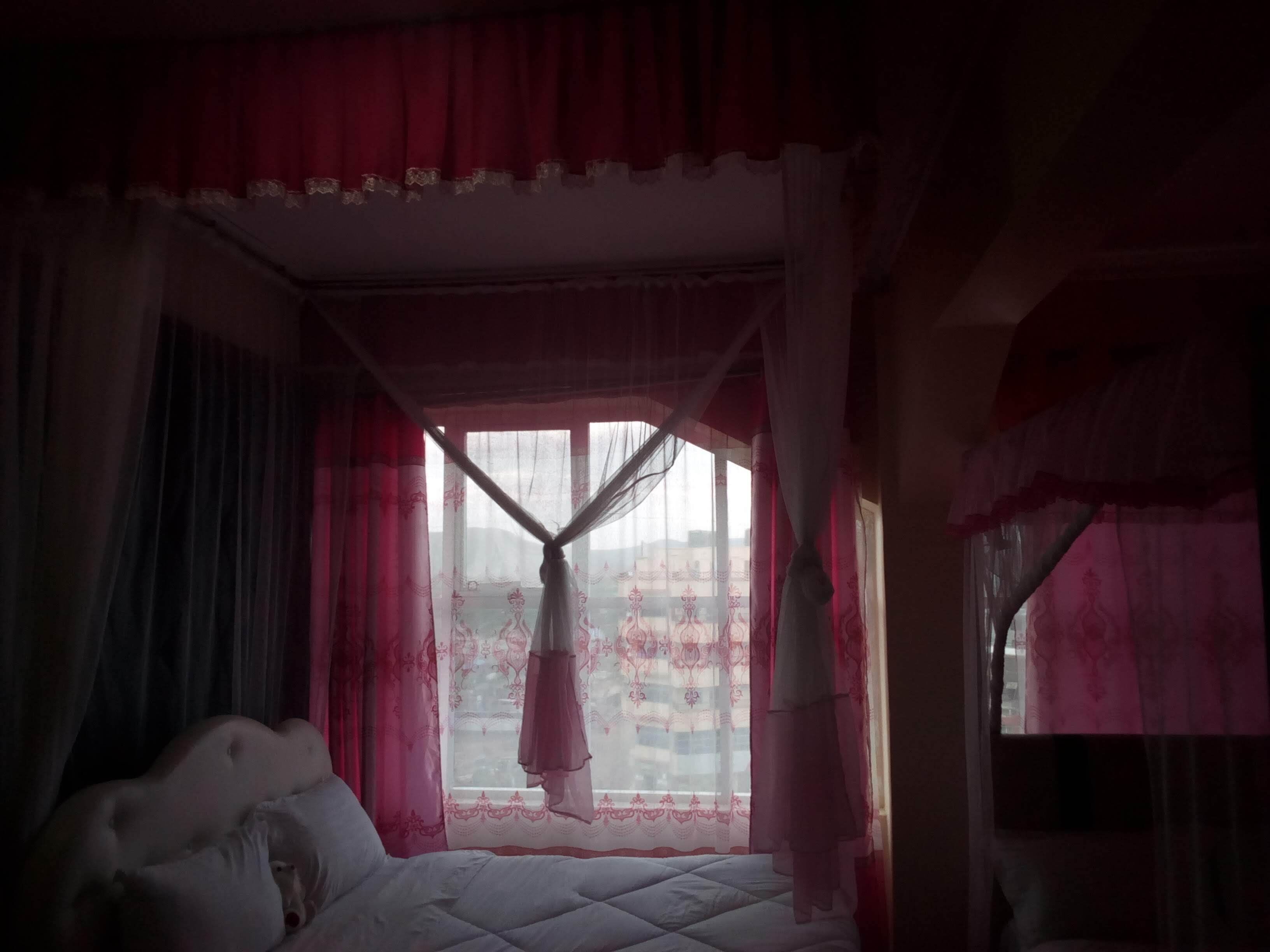 Quarto com cama, cortinas e janela com vista.