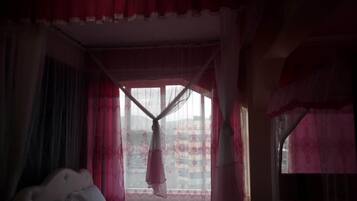 Quarto com cama, cortinas e janela com vista.