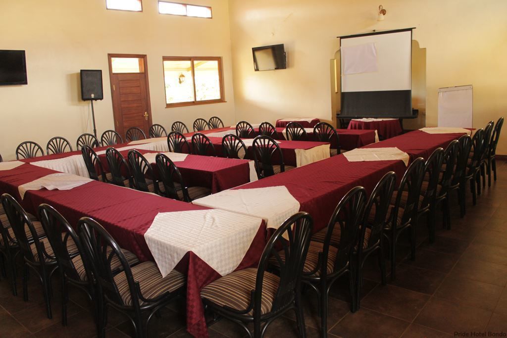 Uma sala de conferências com várias mesas e cadeiras, uma tela de projetor e um quadro branco.
