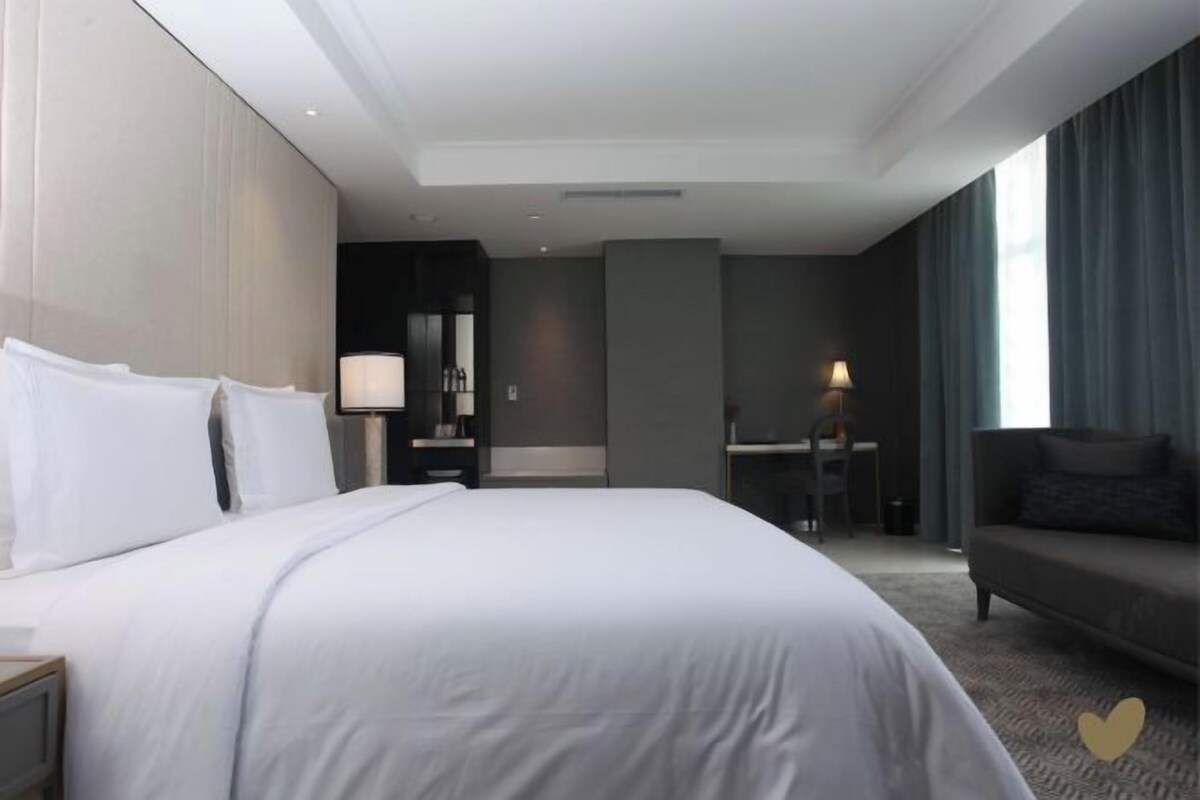 Quarto de hotel moderno com uma cama grande, uma mesa, uma cadeira e um sofá.