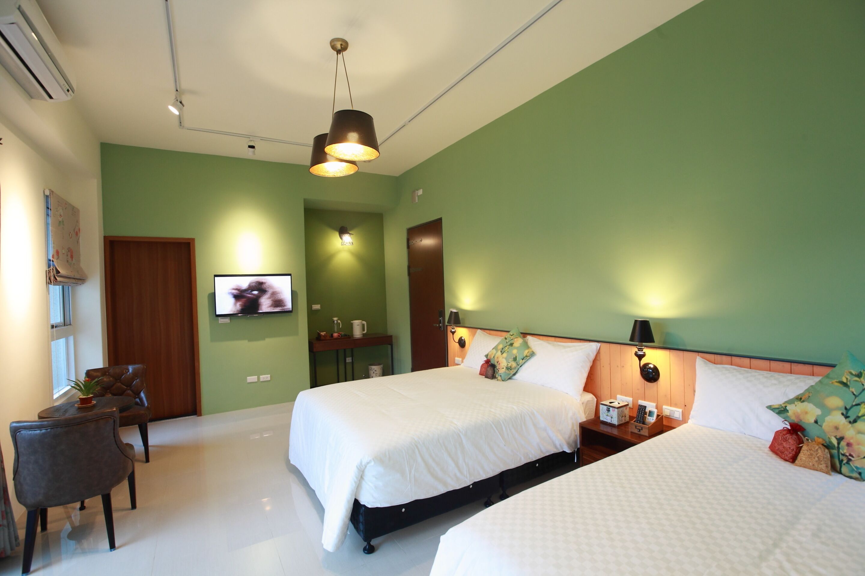 Quarto de hotel com duas camas, televisão, escrivaninha com cadeira e uma pequena mesa com planta.