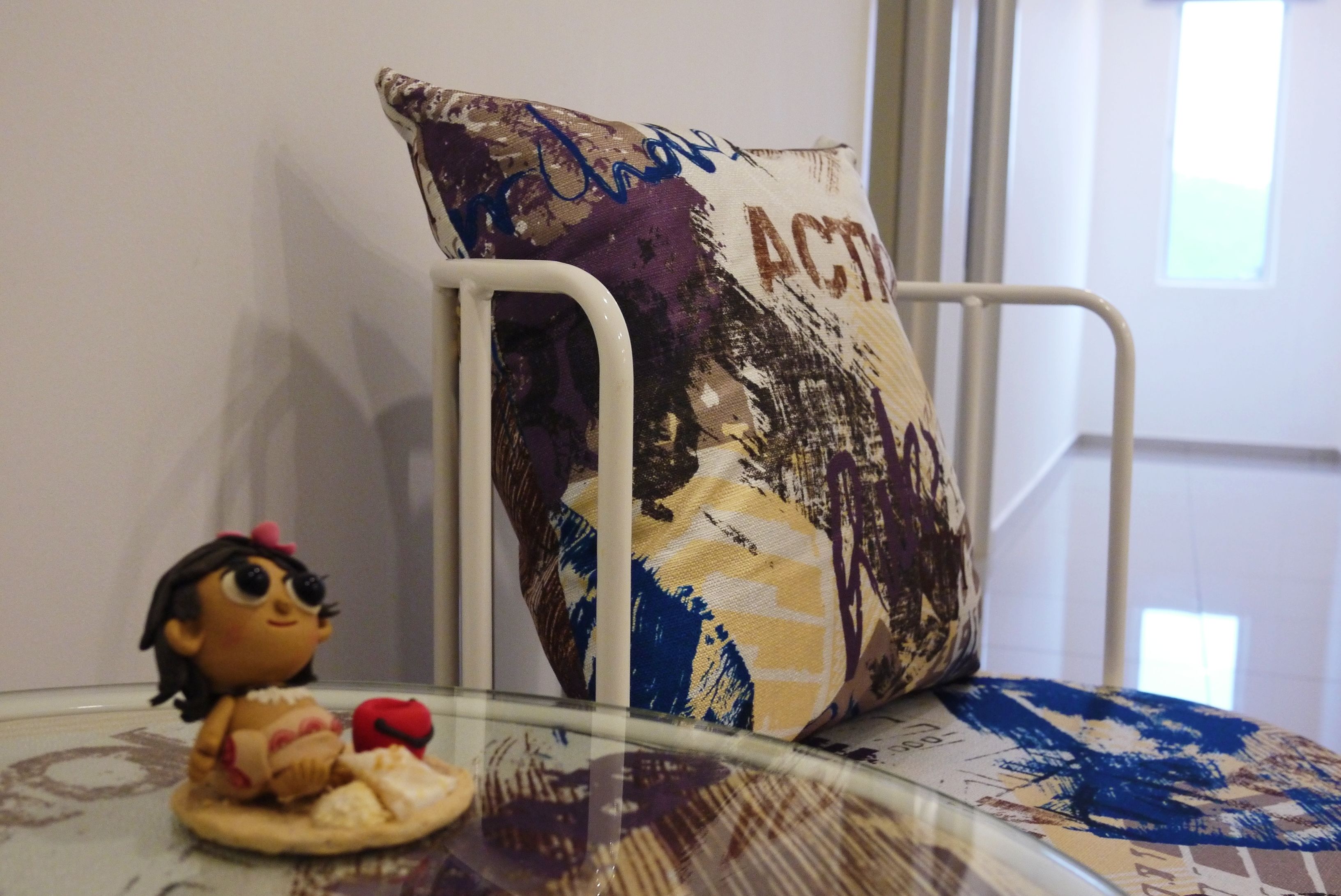Uma mesa de vidro com uma figurina e um travesseiro estampado.