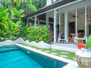 Uma área à beira da piscina com vista desobstruída, um espaço de estar coberto com cadeiras suspensas e vegetação exuberante ao redor.